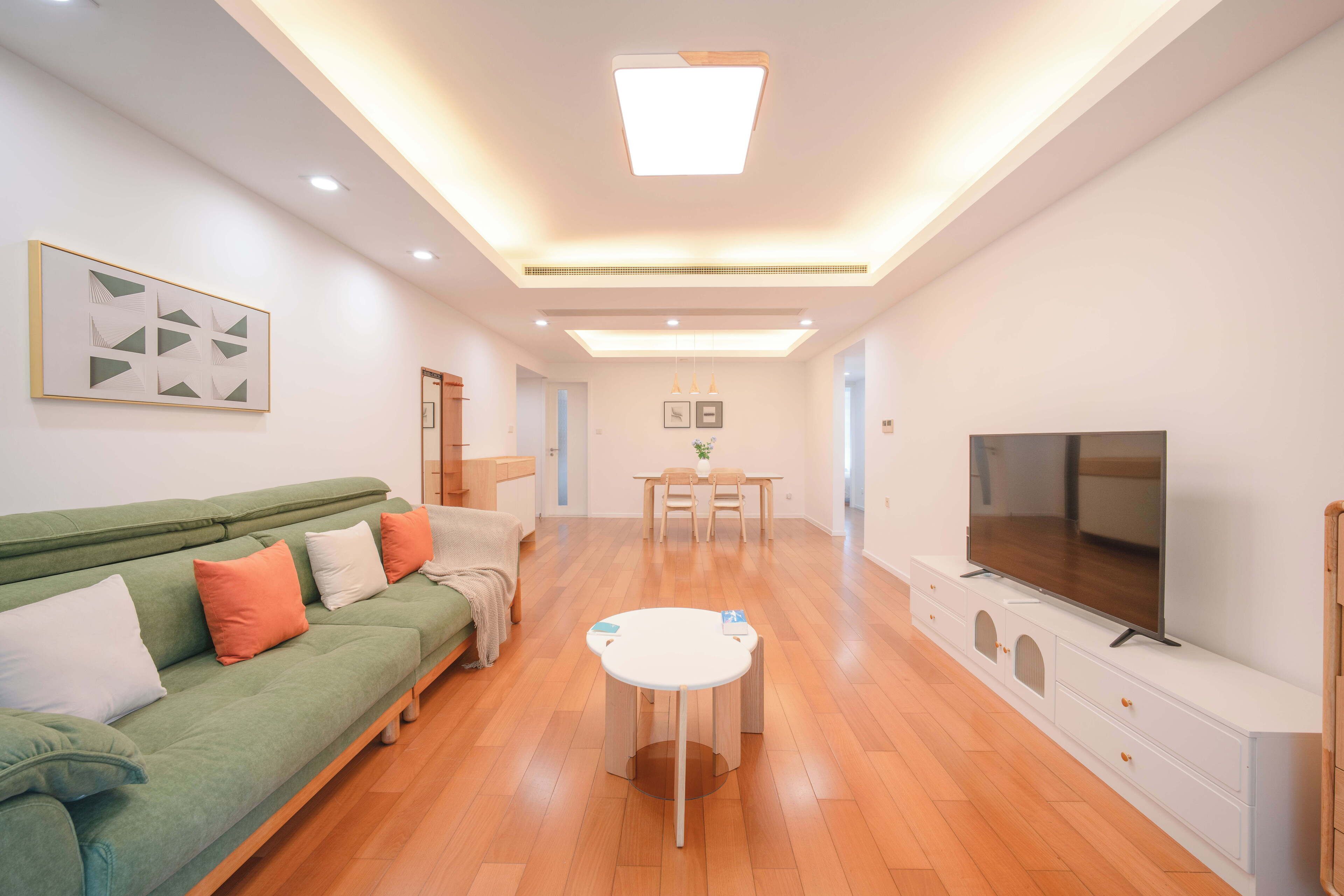 Uma sala de estar moderna com um sofá verde, uma mesa redonda branca e uma televisão em um armário branco.
