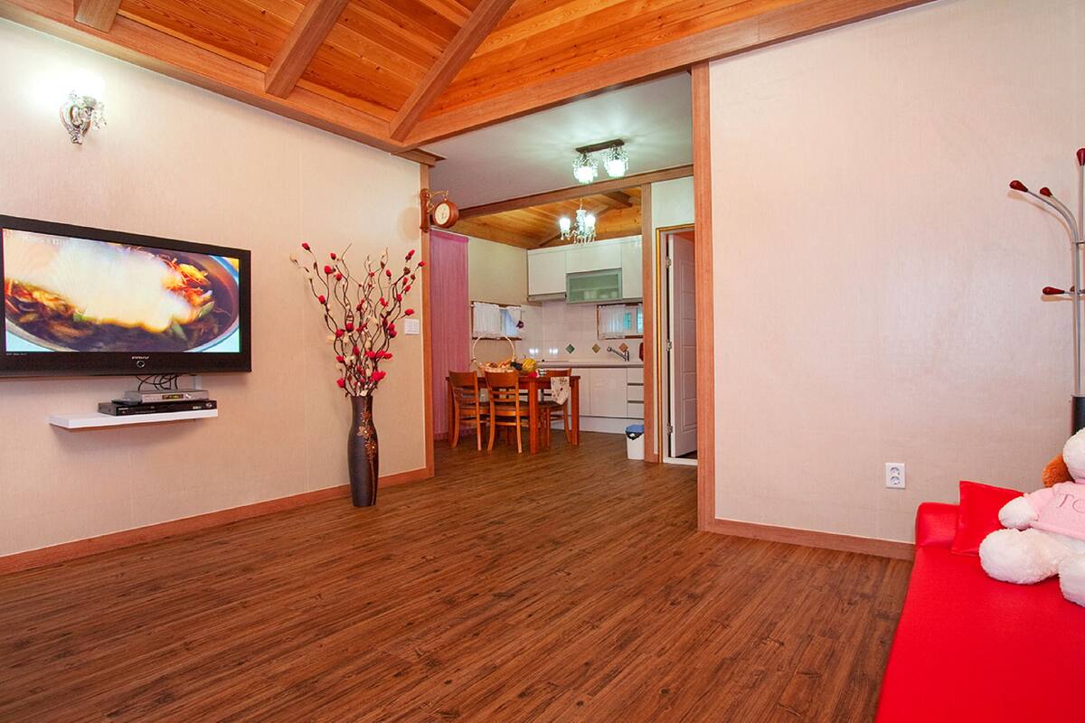 Uma sala de estar com piso de madeira, televisão, vaso com flores e um sofá vermelho.