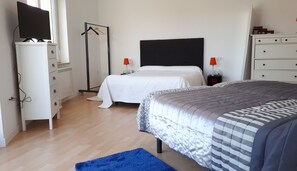 Quarto com duas camas, um guarda-roupa, uma televisão e uma escrivaninha.