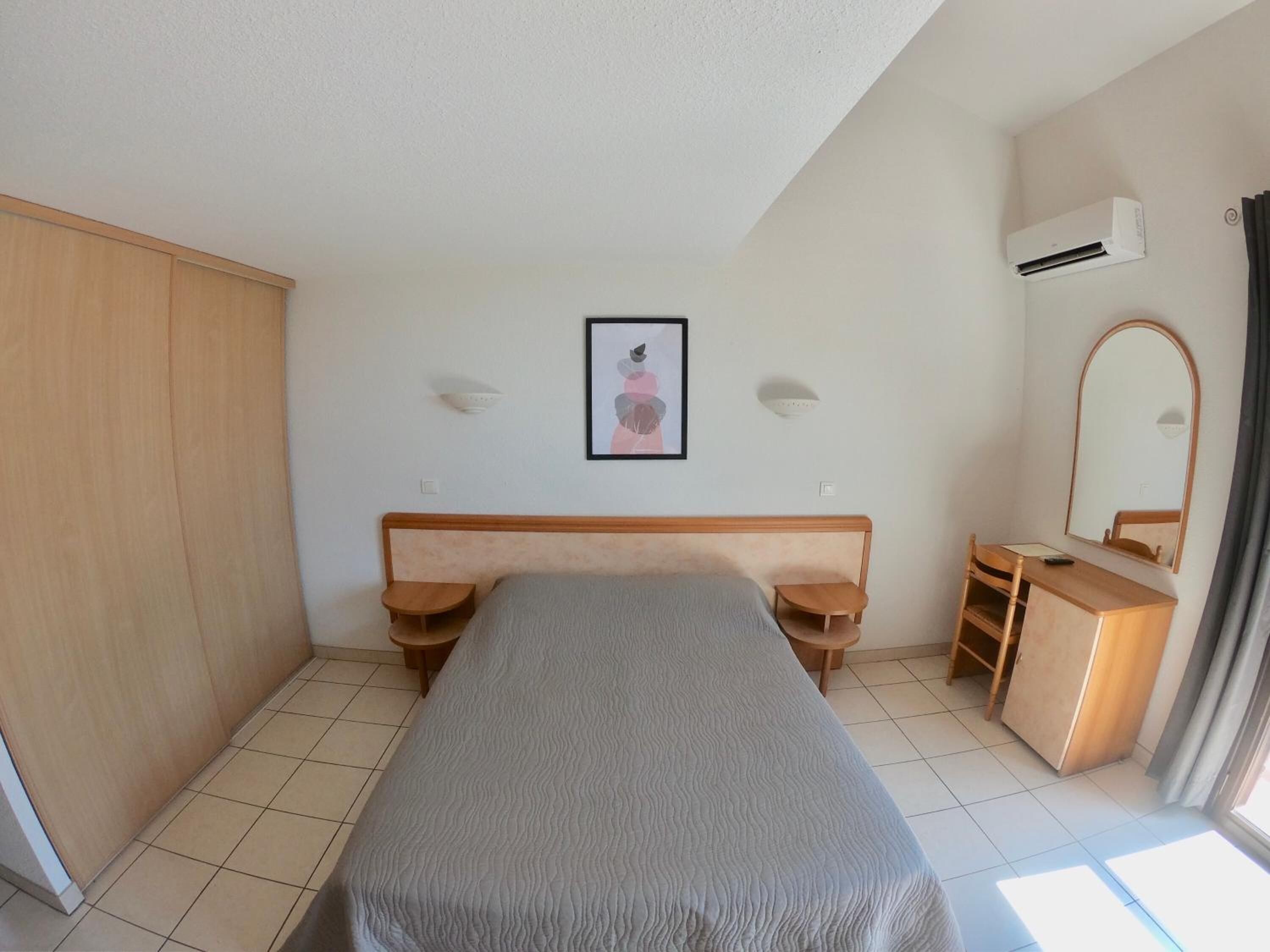 Quarto com cama, escrivaninha, cadeira, guarda-roupa e ar condicionado.