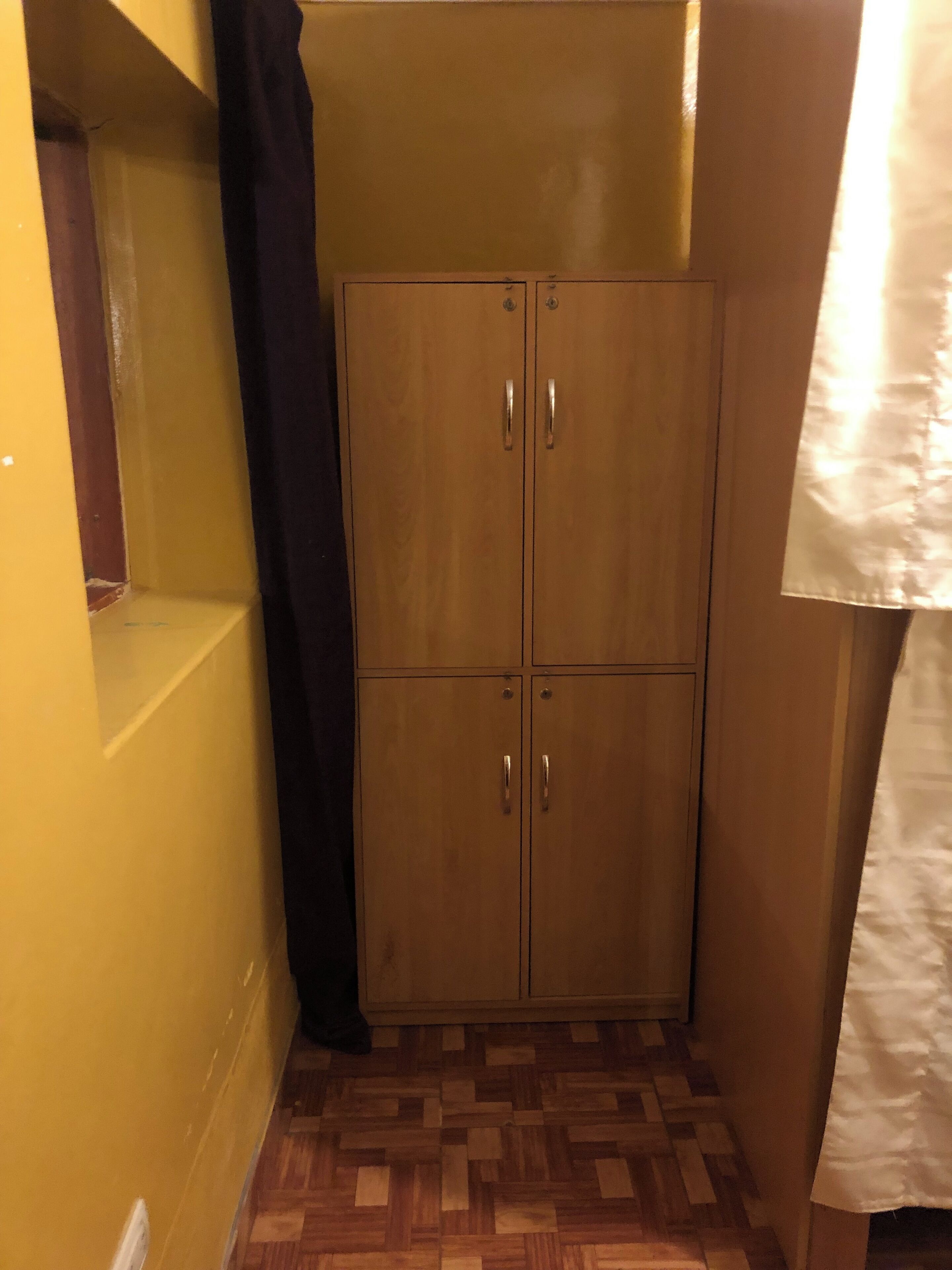 Quarto pequeno com guarda-roupa de madeira, piso de madeira e parede amarela.