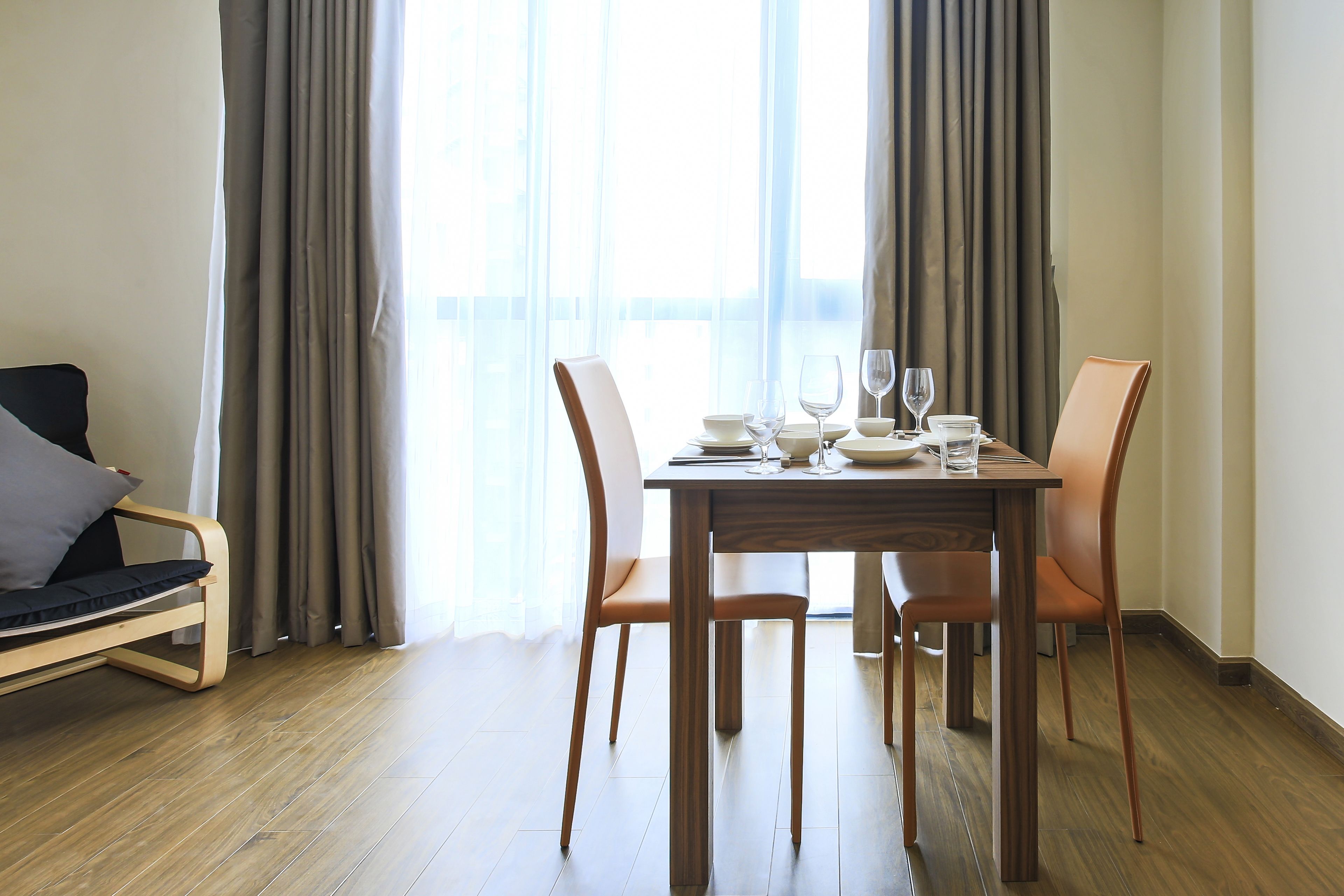 Uma sala de jantar com uma mesa de madeira posta para dois, duas cadeiras e um sofá com almofada.