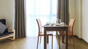 Uma sala de jantar com uma mesa de madeira posta para dois, duas cadeiras e um sofá com almofada.