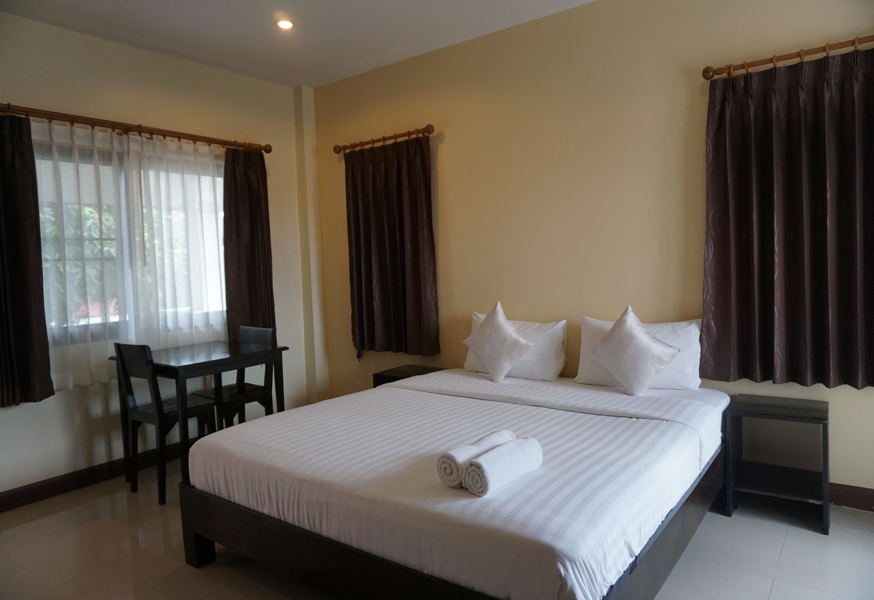 Quarto de hotel com uma cama grande, duas mesas de cabeceira, uma escrivaninha com cadeira e cortinas nas janelas.