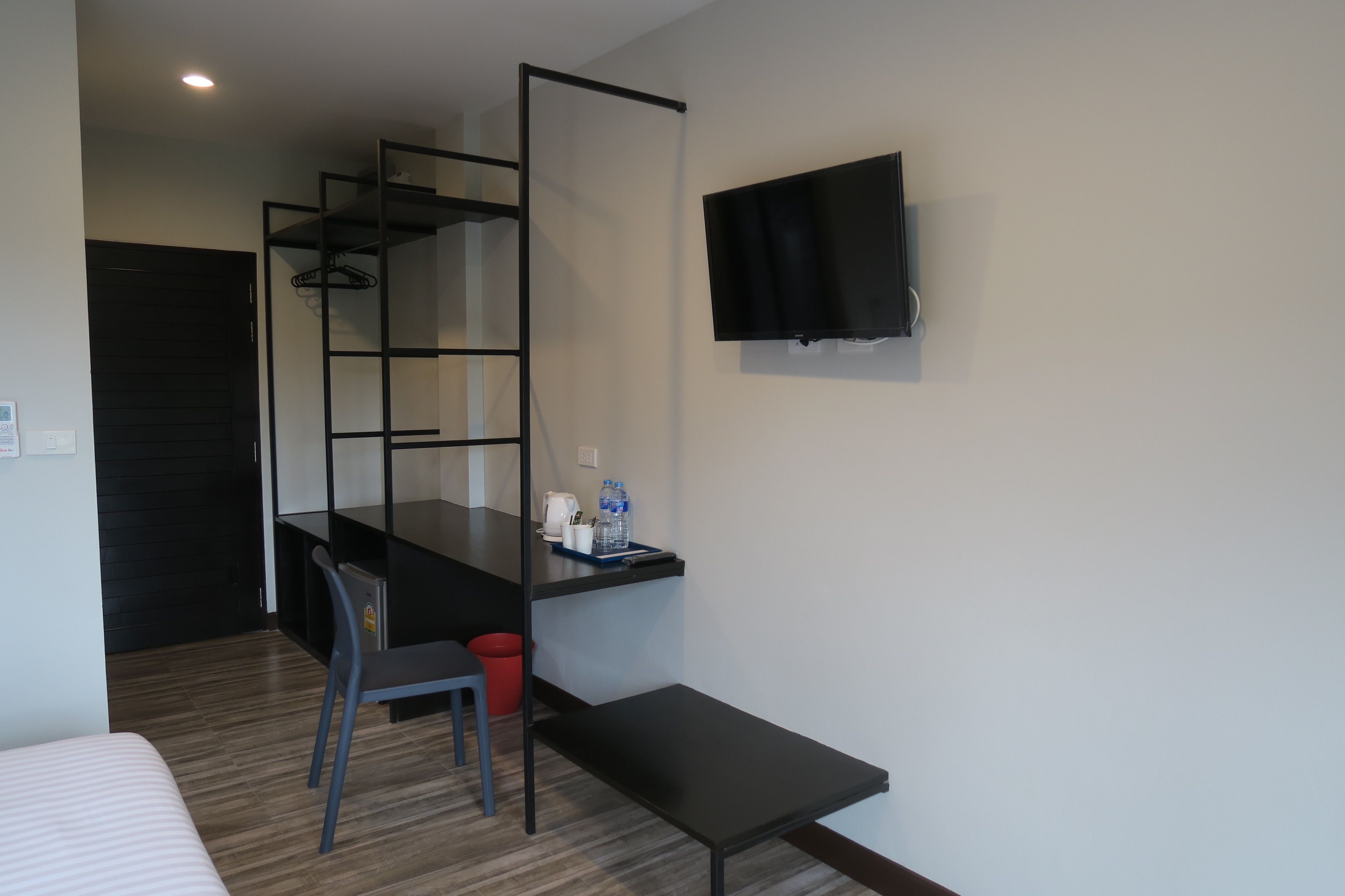 Quarto de hotel com cama, secretária com cadeira, televisão na parede e prateleira com garrafa de água e copo.