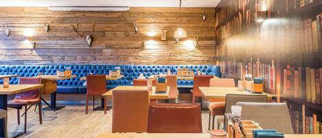Um restaurante moderno com paredes de madeira, assentos acolchoados em azul e uma variedade de mesas e cadeiras.