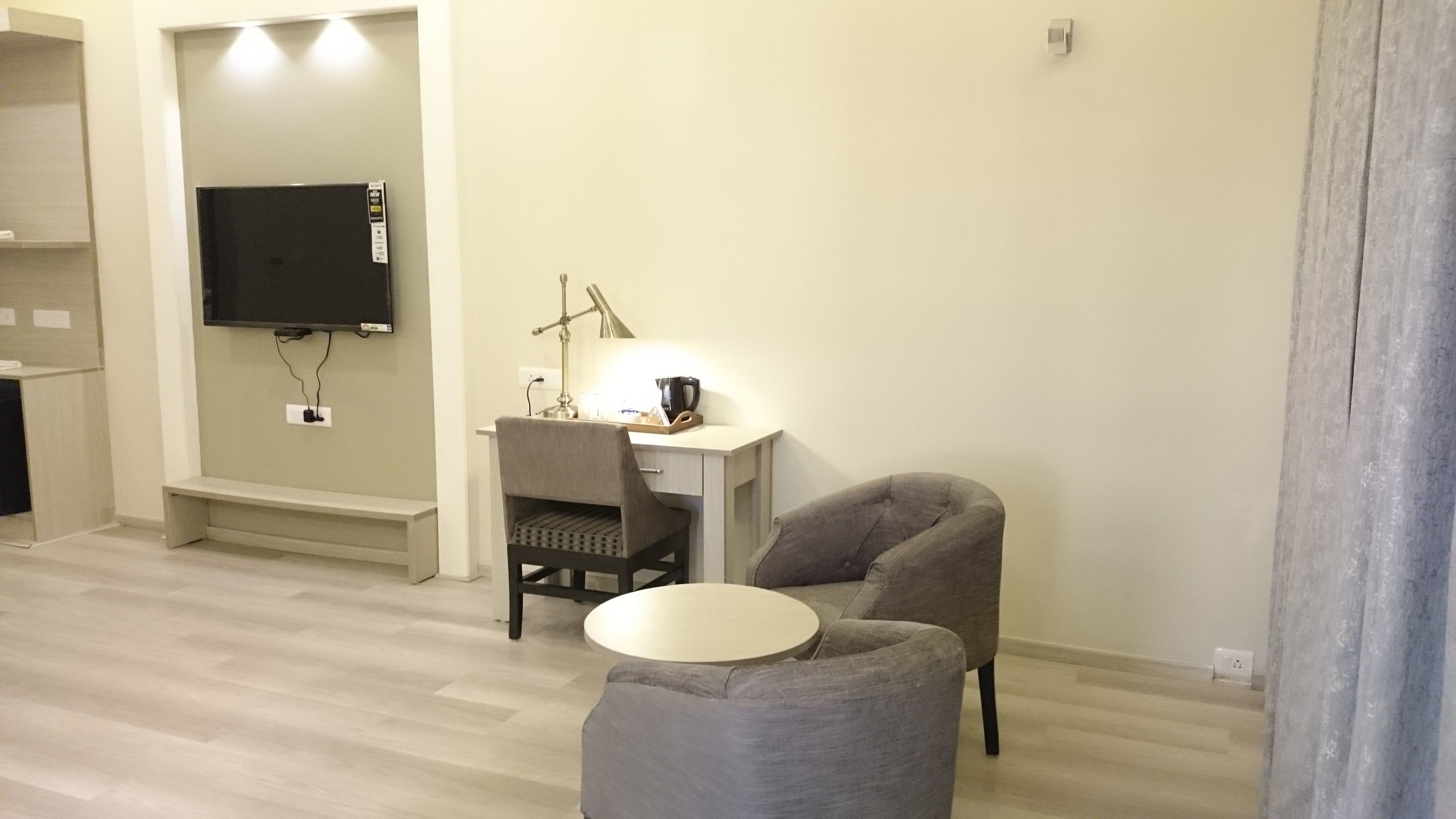 Uma sala de estar moderna com televisão de tela plana na parede, uma escrivaninha com cadeira, uma mesa de centro redonda e uma poltrona cinza.