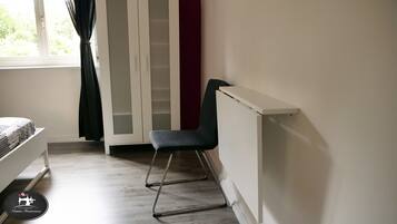 Um quarto com cama, uma cadeira, radiador e janela com cortinas.