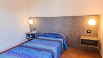 Quarto pequeno com uma cama de solteiro, cabeceira cinza, mesas de cabeceira com luminárias e colcha listrada em azul.