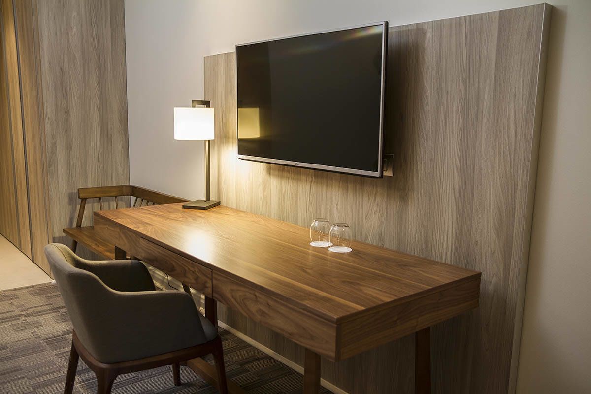 Quarto de hotel moderno com mesa de jantar de madeira, duas cadeiras, televisão de tela plana na parede e abajur.