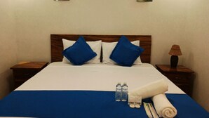 Cama bem arrumada com roupa de cama azul e branca, duas almofadas azuis, um painel de cabeceira de madeira e uma mesa de cabeceira com abajur.