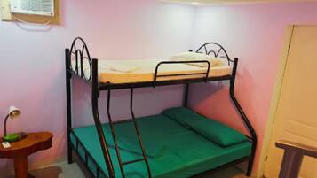 Uma cama beliche com colchão verde, uma mesinha com luminária e um ar condicionado fixado na parede.