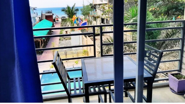 Uma varanda com mesa e cadeiras, com vista para uma rua com prédios e o mar.