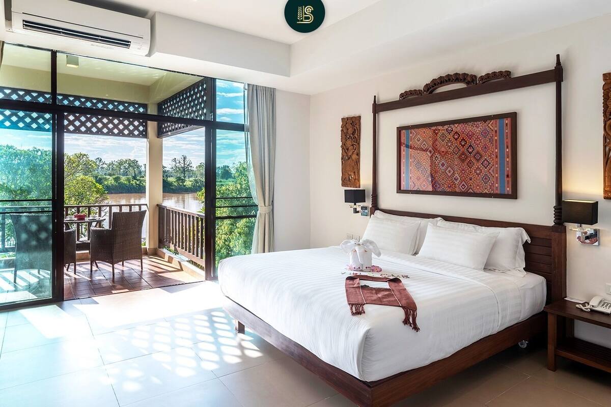 Quarto de hotel com uma cama grande, varanda com vista e cabeceira de madeira.