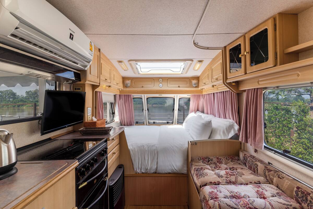 Interior compacto de uma RV com cozinha compacta, uma cama com almofada estampada e uma televisão.