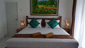 Uma cama bem arrumada com cabeceira marrom, dois travesseiros decorativos e duas toalhas enroladas.
