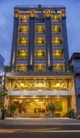 Um hotel de vários andares com uma placa de destaque que diz "HUONG SEN HOTEL II". O edifício apresenta varandas ornamentadas com grades de metal e plantas em vasos.