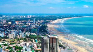 Paisagem costeira com praia, edifícios altos e céu claro.