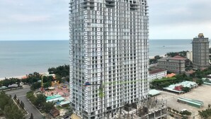 Um edifício alto com vários andares, rodeado por uma área de construção e um corpo de água ao fundo.