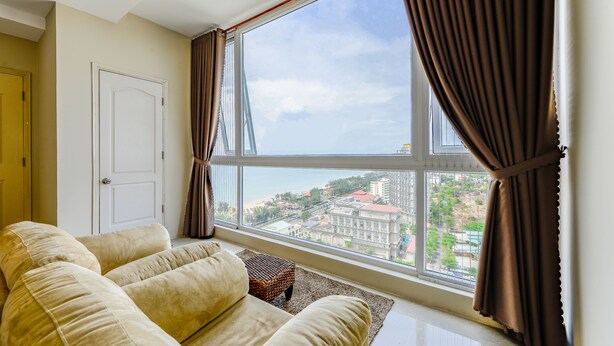 Sala de estar com uma janela grande, sofá bege e vista para a paisagem urbana.