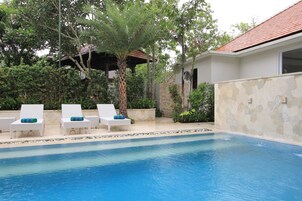 Piscina com espreguiçadeiras e área coberta, rodeada por vegetação e uma parede de pedra.