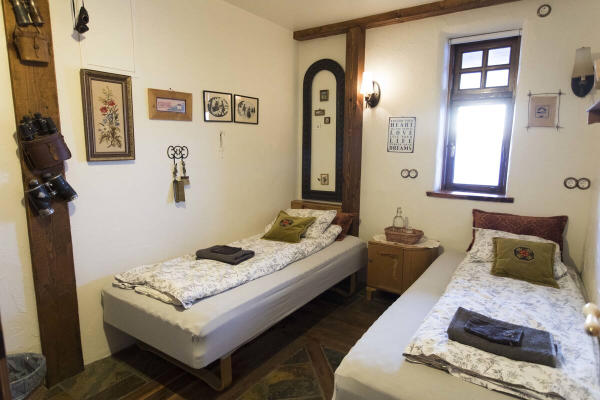 Um quarto pequeno e acolhedor com duas camas individuais, um guarda-roupa de madeira, um espelho e uma janela com vista.