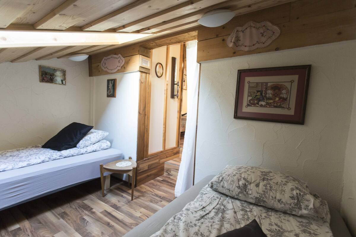 Um quarto pequeno e acolhedor com duas camas, piso de madeira e uma pequena mesa.