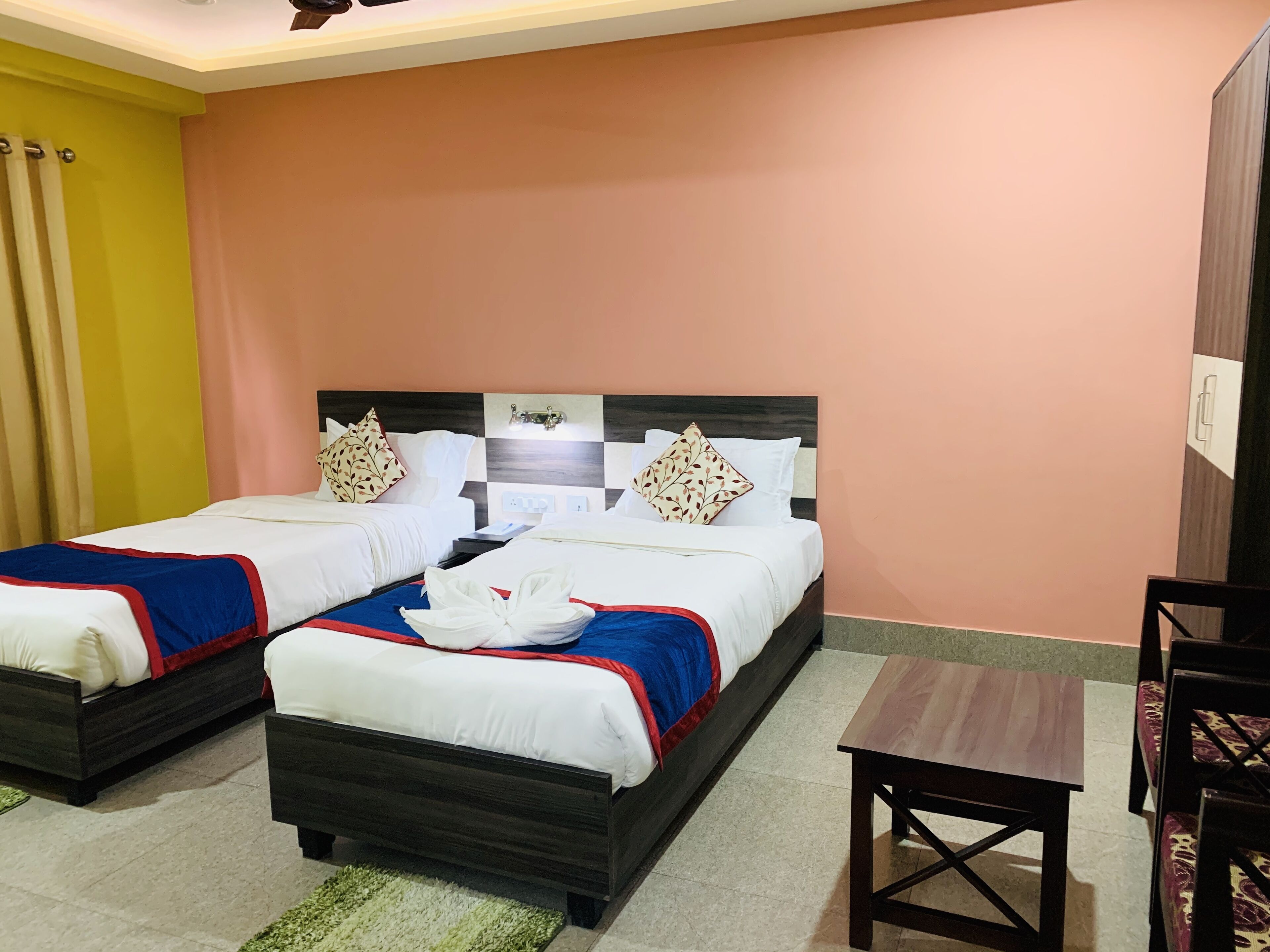 Quarto de hotel com duas camas, uma mesa pequena e uma cadeira.