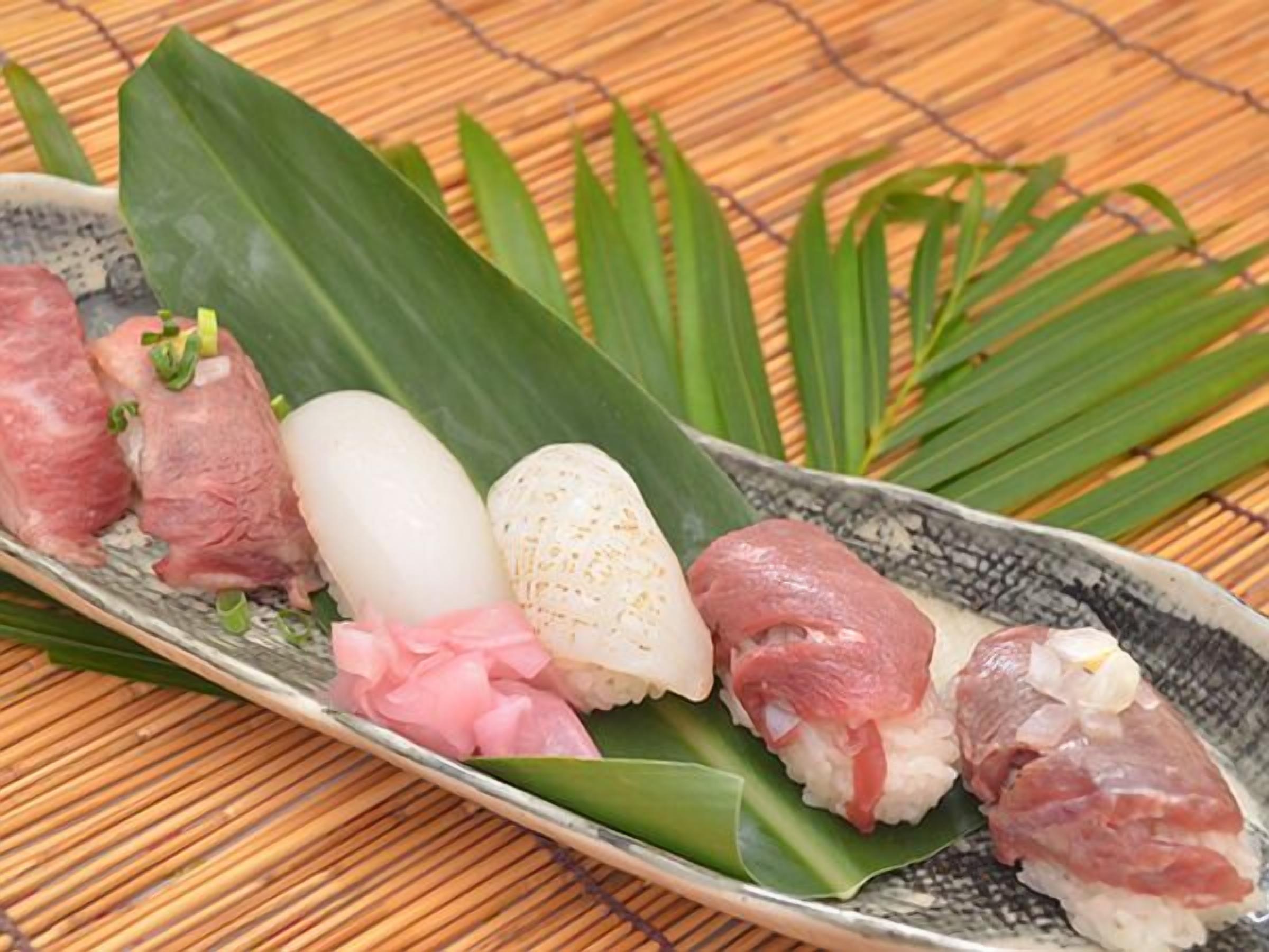 Uma seleção de sushi em um prato de cerâmica, decorada com folhas verdes e gengibre rosa em conserva.