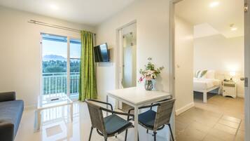 Quarto de hotel moderno com varanda, área de refeições com mesa e cadeiras, cama com mesa de cabeceira e televisão na parede.