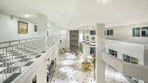 Um interior em vários níveis com piso xadrez, corrimãos brancos e um pilar decorativo central com lanternas penduradas.