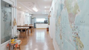 Um quarto espaçoso com piso de madeira, um grande mapa na parede e uma área de jantar com mesas e cadeiras.