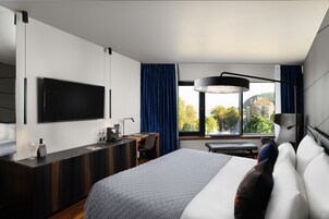 Quarto de hotel moderno com uma cama grande, uma escrivaninha, televisão de tela plana e vista para a cidade pela janela.