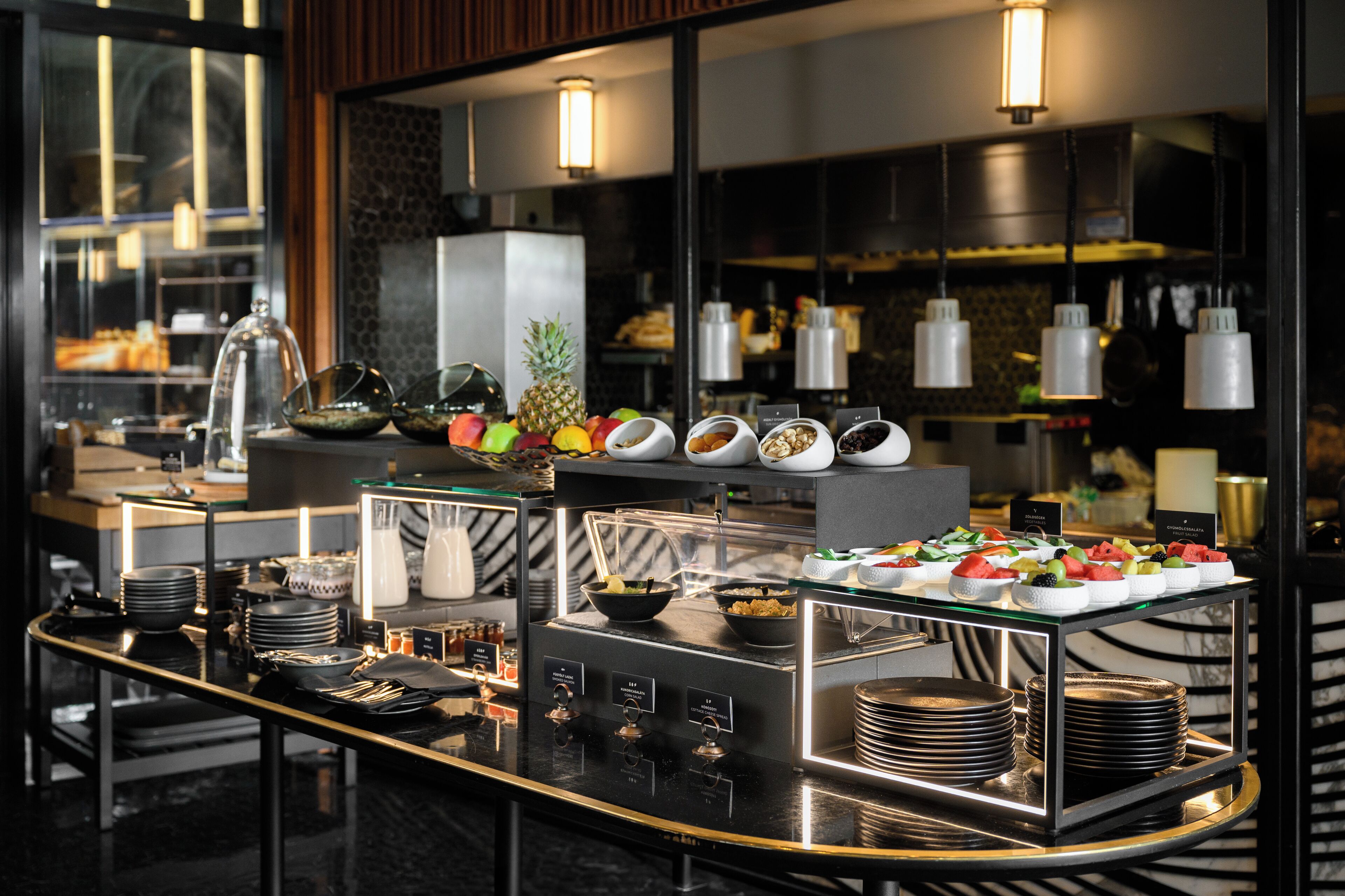 Buffet com diversos alimentos, acompanhamentos, máquina de café e vitrine de vidro.