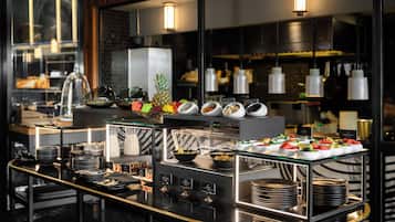 Buffet com diversos alimentos, acompanhamentos, máquina de café e vitrine de vidro.