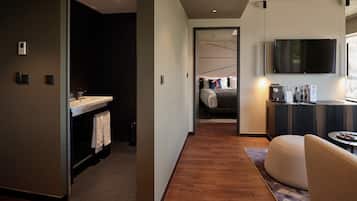 Quarto de hotel moderno com piso de madeira, uma cama grande, televisão e minibar.