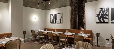Um restaurante com mesas preparadas para refeições, cadeiras de madeira e obras de arte nas paredes.
