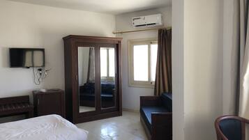 Quarto de hotel com uma cama, um guarda-roupa, uma televisão na parede, uma janela com cortinas e um aparelho de ar condicionado.