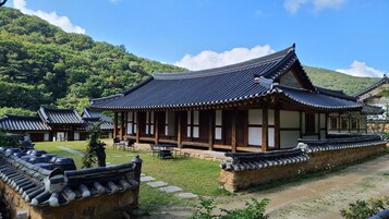 Um edifício tradicional coreano com telhado telhado e estrutura de madeira, cercado por um jardim bem cuidado e um muro de pedra.
