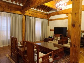 Um quarto com painéis de madeira, uma mesa com tampo de vidro, cadeiras, um sofá e uma televisão.