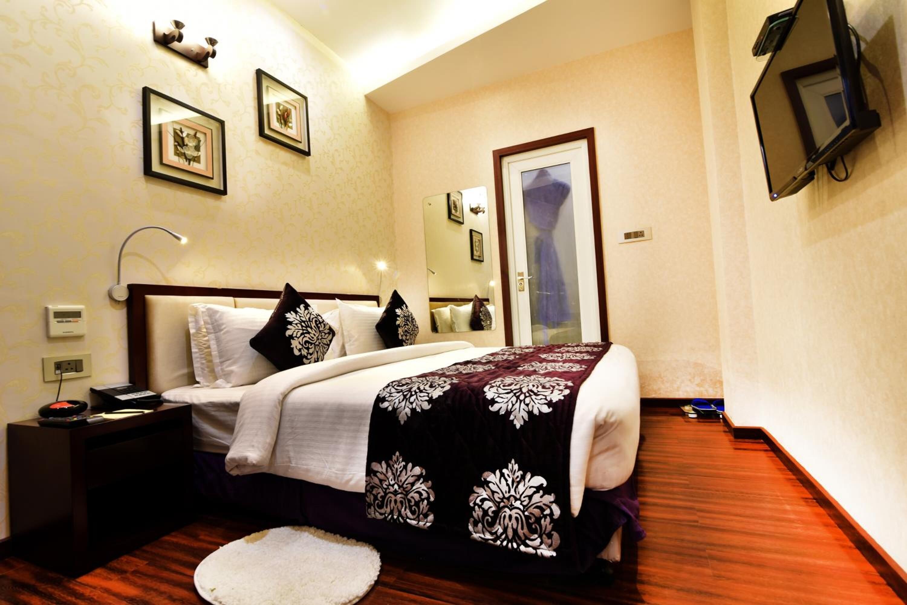 Quarto bem arrumado com cama, mesas de cabeceira, espelho e quadros nas paredes.
