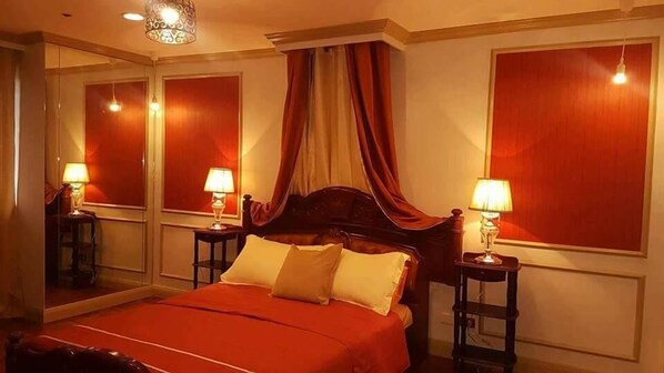 Quarto de hotel com uma cama grande, duas mesas de cabeceira com luminárias, uma cama com dossel e um espelho na parede.