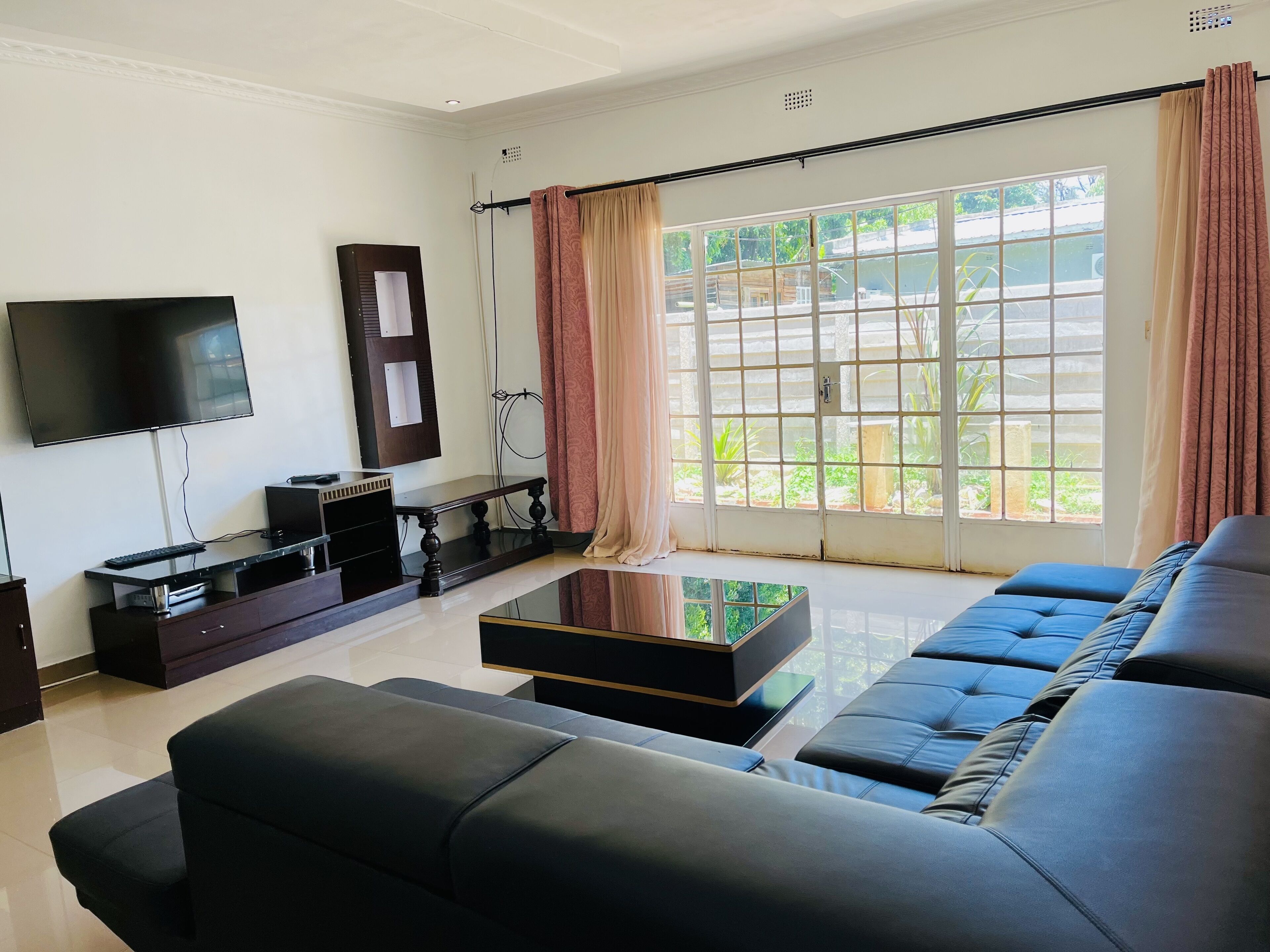 Uma sala de estar moderna com televisão de tela plana, mesa de centro, sofá e uma grande janela com cortinas.