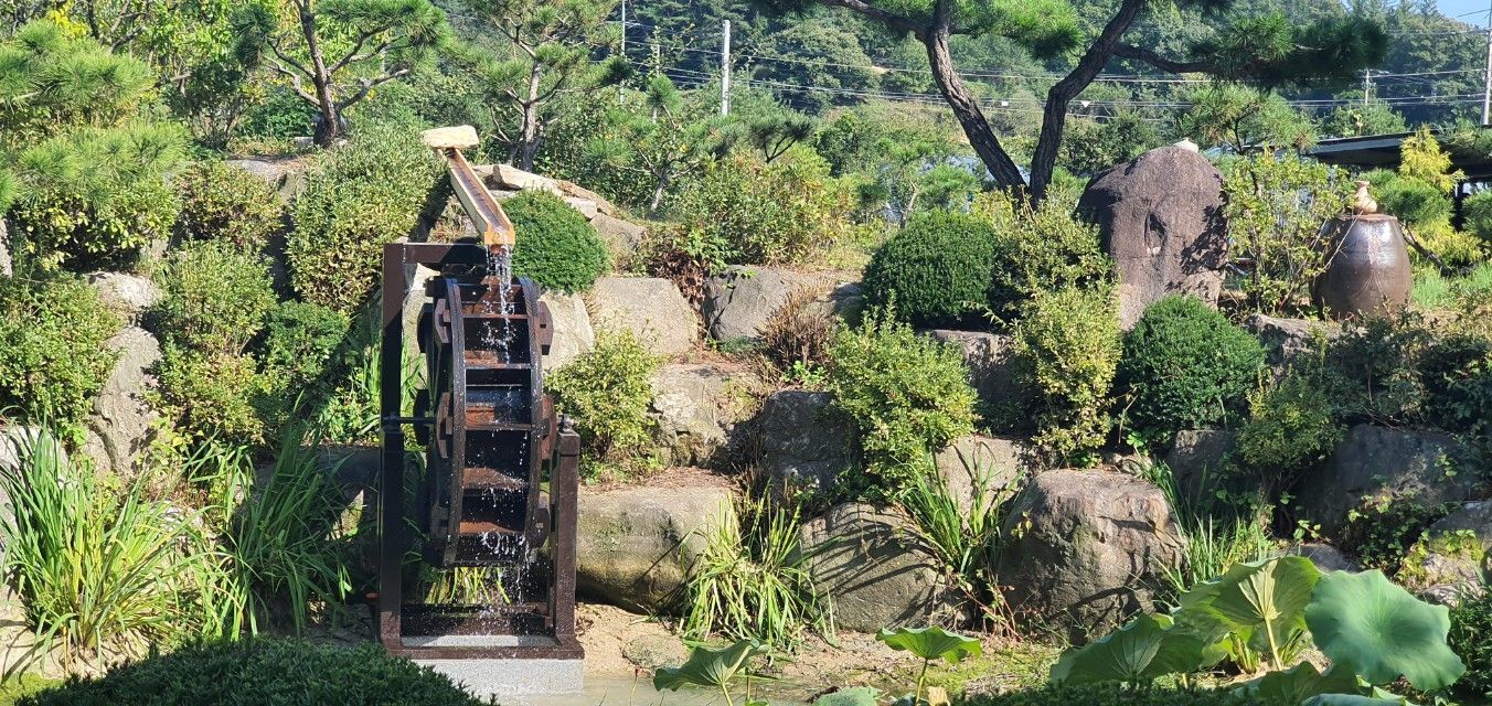 Estrutura tradicional de bomba de água num jardim, com pedras e vegetação.