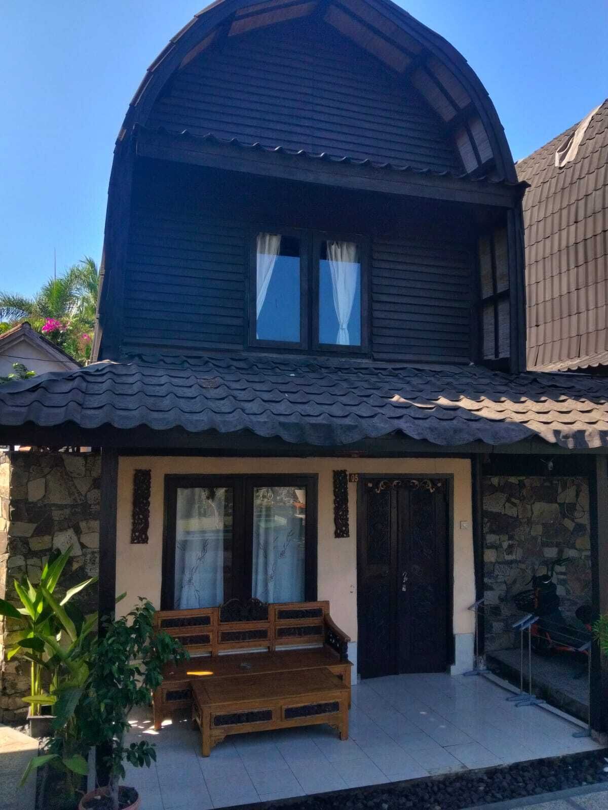 Uma casa de dois andares com telhado de telhas, fachada de pedra e um banco de madeira na parte externa.