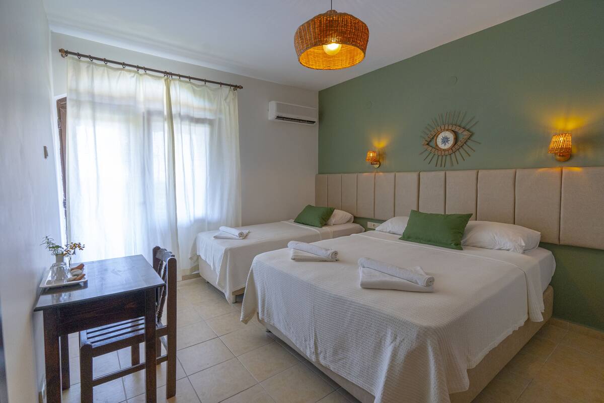 Quarto de hotel com duas camas, uma mesa de jantar e uma janela com cortinas.
