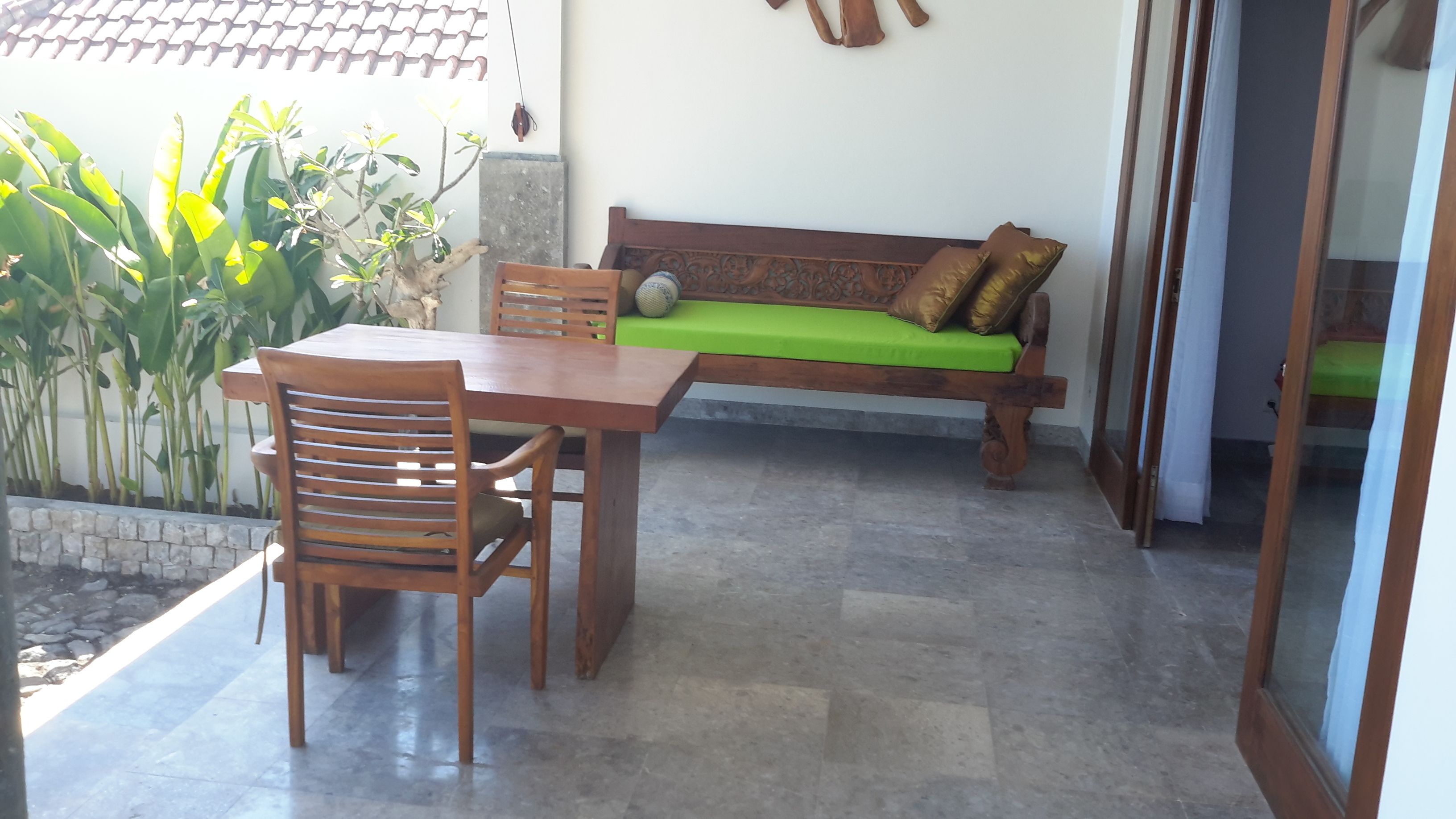 Uma mesa e cadeiras de madeira, um sofá com almofadas verdes e um vaso de pedra com plantas.