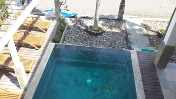Piscina retangular com deck de madeira ao redor, caminho de pedra e alguns vasos com plantas.