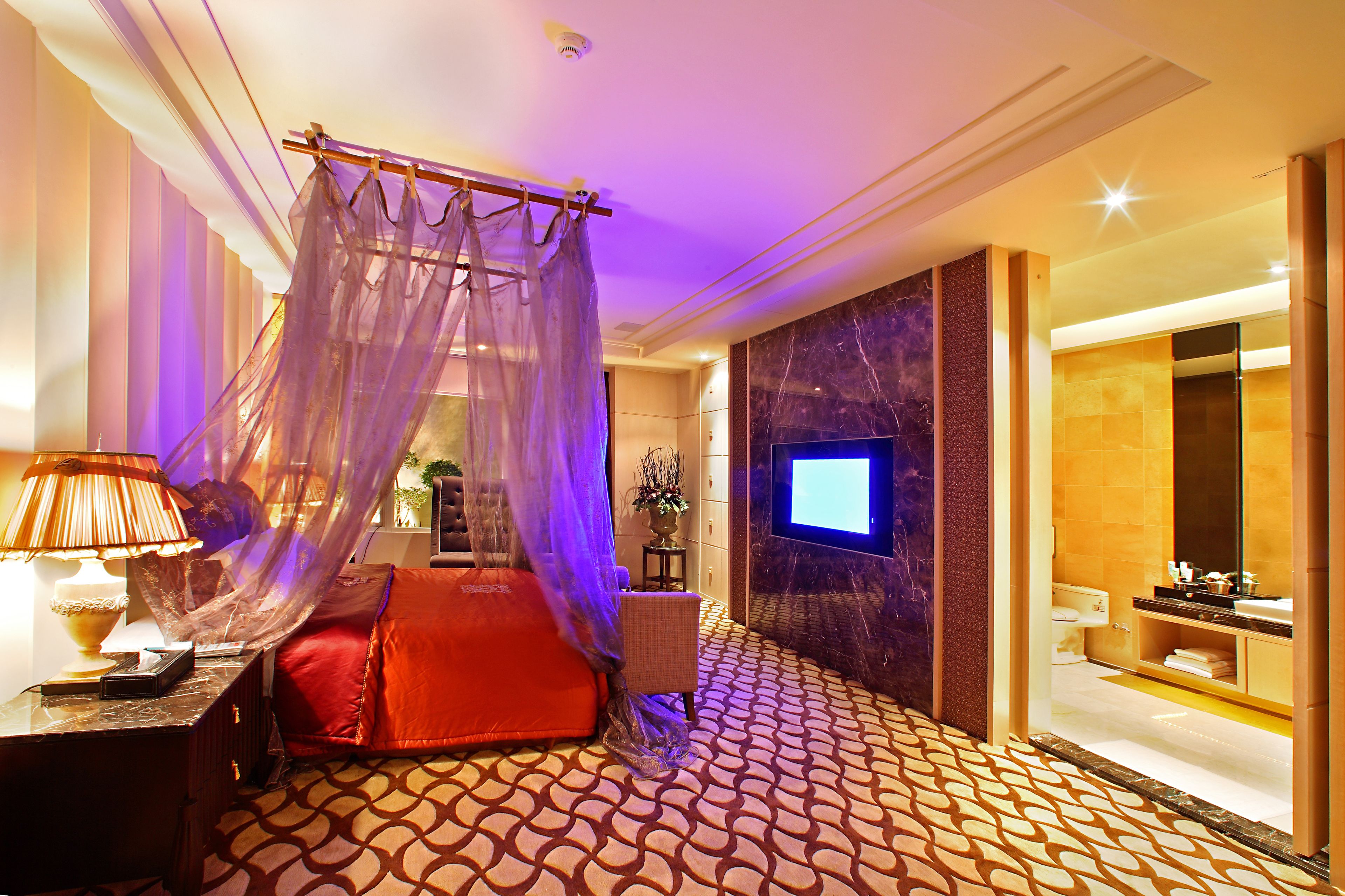 Quarto de hotel com cama, televisão, banheiro e piso estampado.
