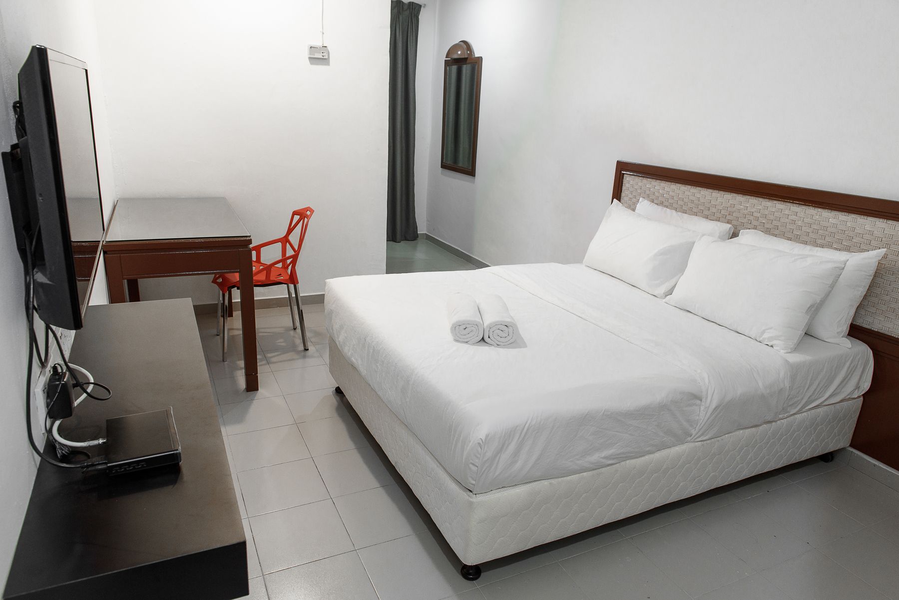 Quarto de hotel com uma cama, uma escrivaninha com cadeira, uma televisão e um espelho.